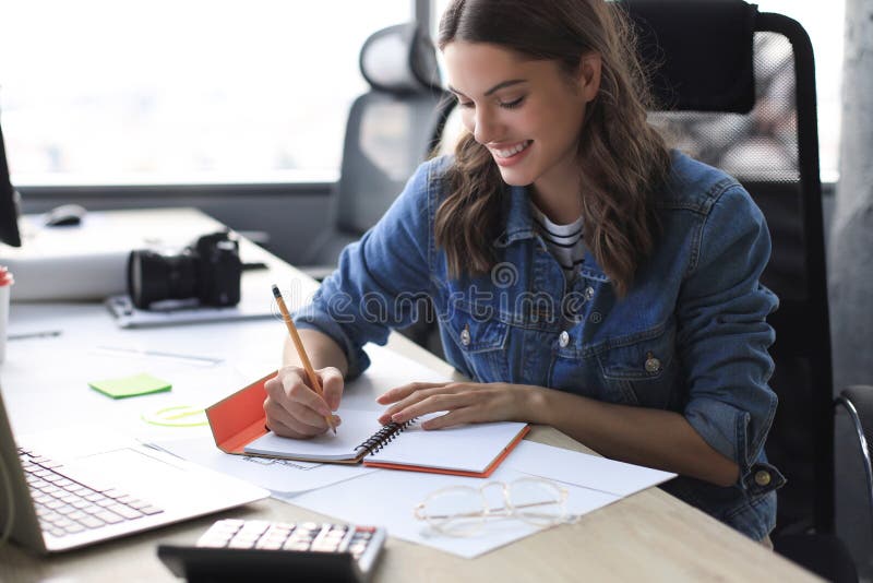 Happy Young Woman Writing Something Down while Working in the Office ...