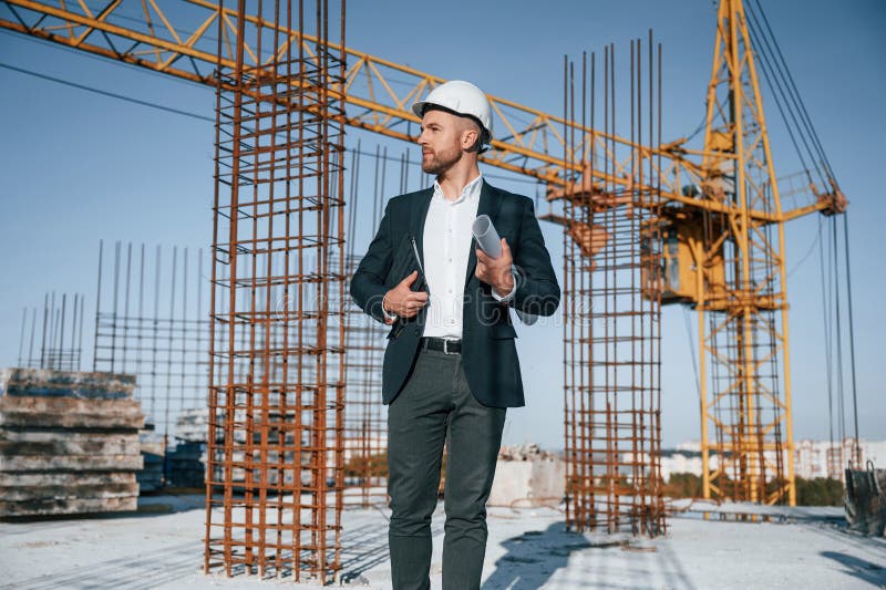 In Hard Hat, Holding Plan in Hands. Businessman in Formal Clothes is on ...