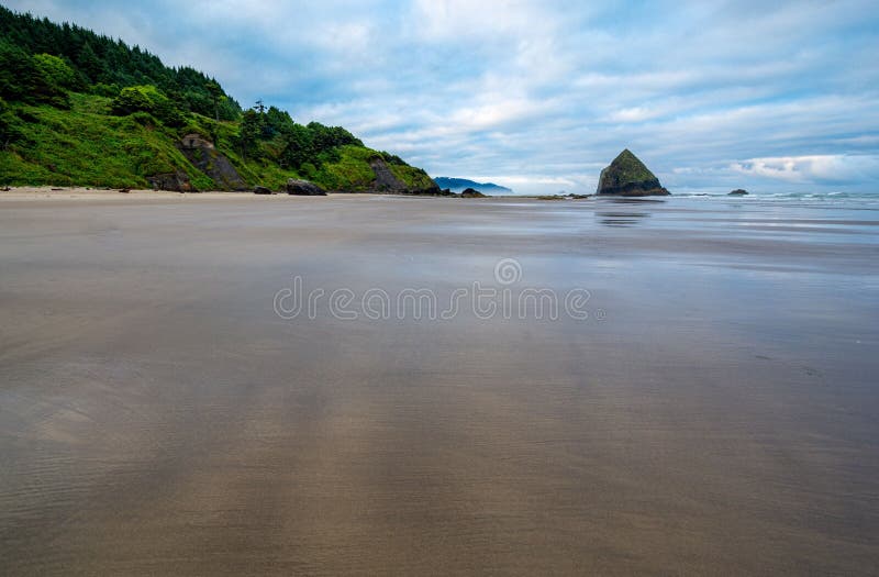 Haystack Rock, Green Rocky Cliffs and Wet Sand on Cannon Beach Under ...