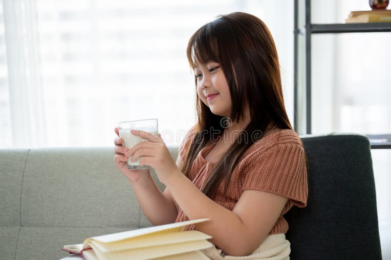 A Healthy And Adorable Young Asian Girl Drinking Milk From A Glass On A