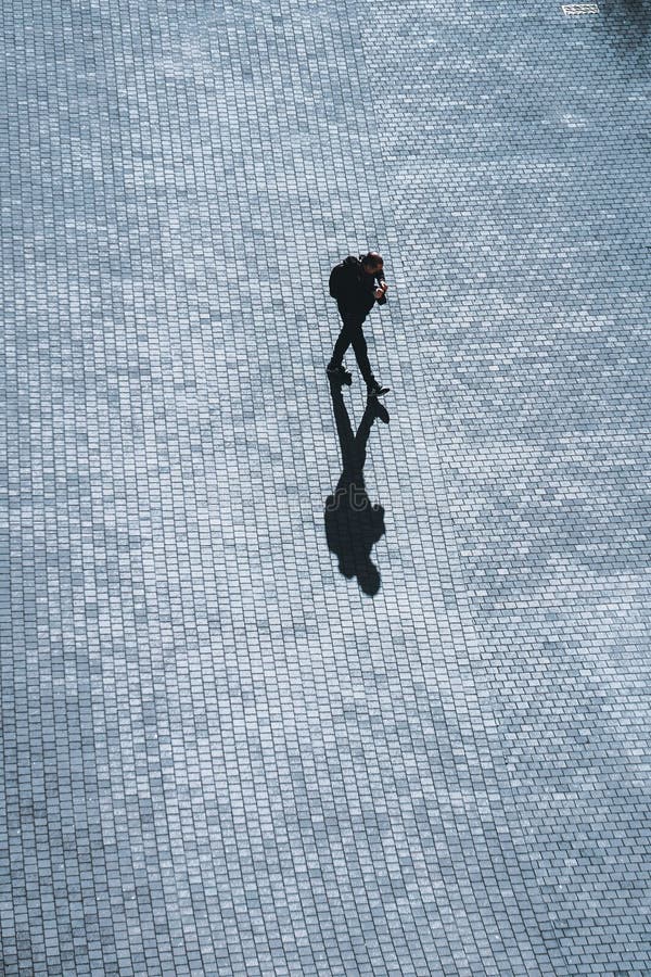 High Angle Shot of a Pedestrian Walking with a Shadow on a Cobblestone ...