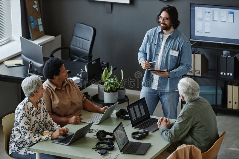 Bearded Young Man Leading Computer Class for Seniors Using Laptops at ...