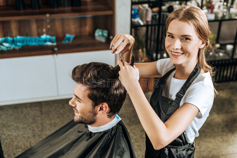 High Angle View of Hairstylist Smiling at Camera while Cutting Hair To ... High Angle View of Hairstylist Smiling at Camera while Cutting Hair To ...