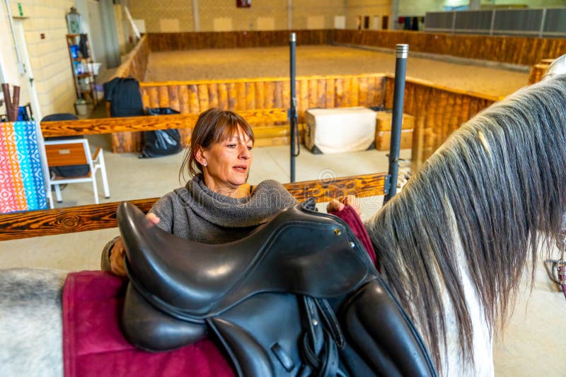 A Woman Saddling a Horse in Stable Stock Photo - Image of horizontal ...