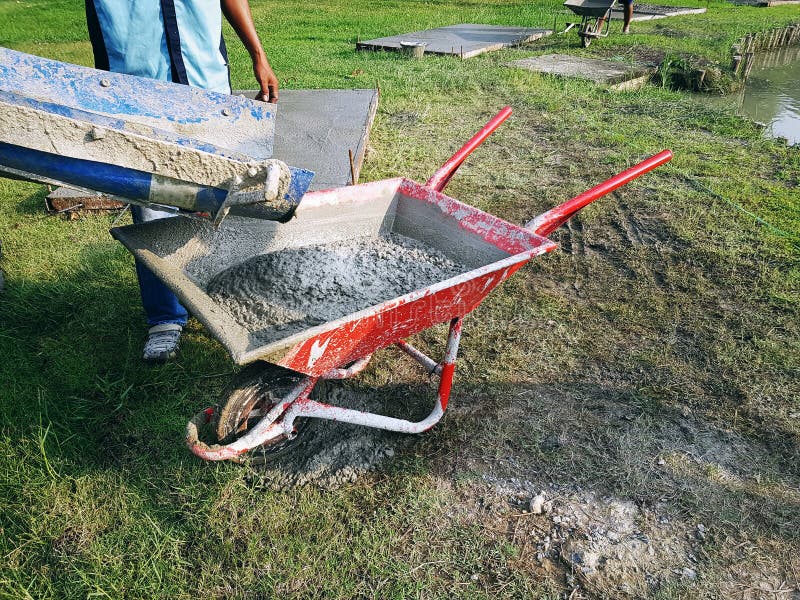 Worker Pouring Mixed Cement into Red Wheelbarrow at Construction Site ...