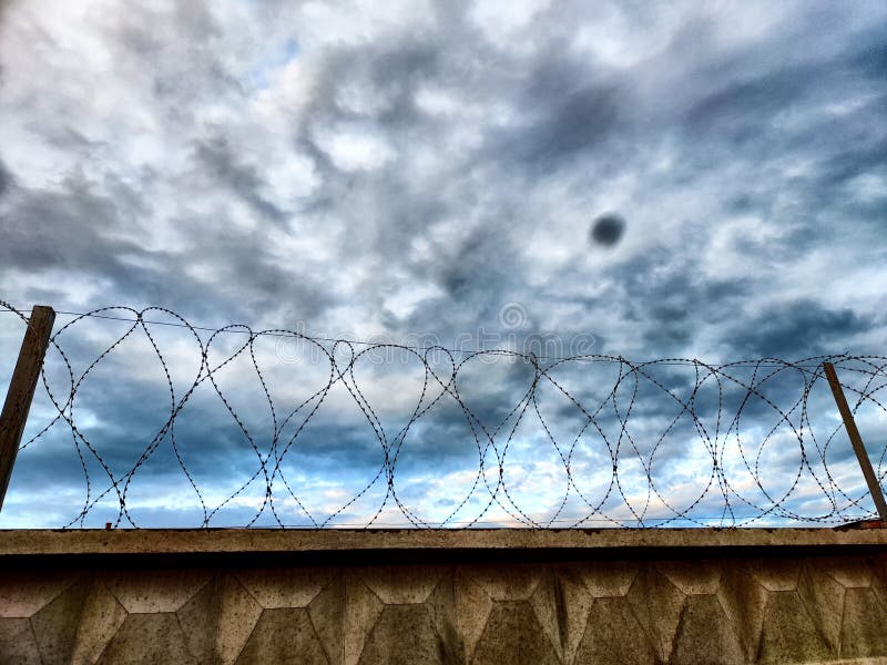 High Concrete Wall and Fence with Barbed Wire on Background of Sky with ...