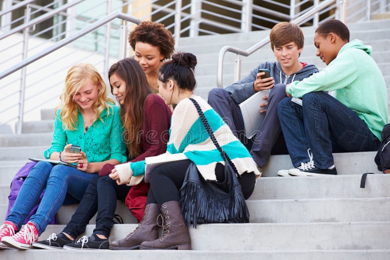 High School Students Sitting Outside Building with Phones Stock Photo ...
