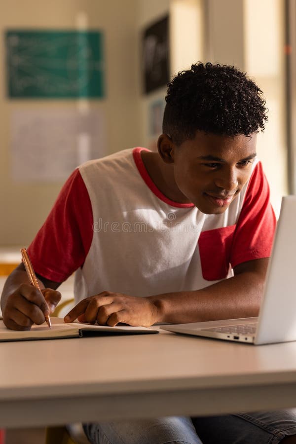 In High School, Teenage Boy Writing in Notebook while Using Laptop in ...