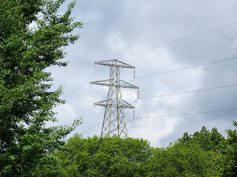 A High-voltage Power Lines Tower Above Lush Green Trees Under a Cloudy ...