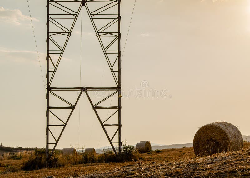 High Voltage Pylon in a Mowed Field with Straw Rollers at Sunset ...