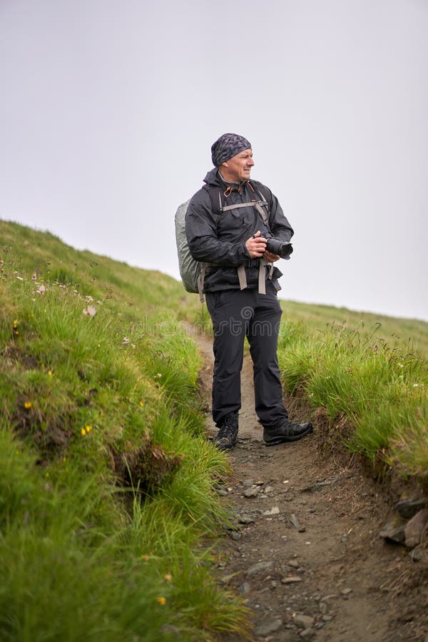 Hiker Man in a Red Raincoat Stands on a Trail in the Mountains,looks in ...