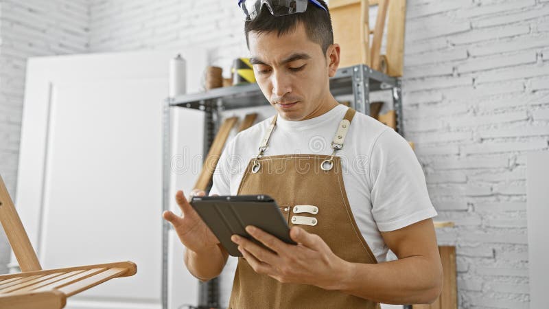 Hispanic Carpenter Using Tablet in a Well-equipped Workshop, Embodying ...