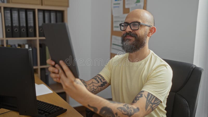Hispanic Man with a Beard and Tattoos, Sitting in an Office, Looks at a ...