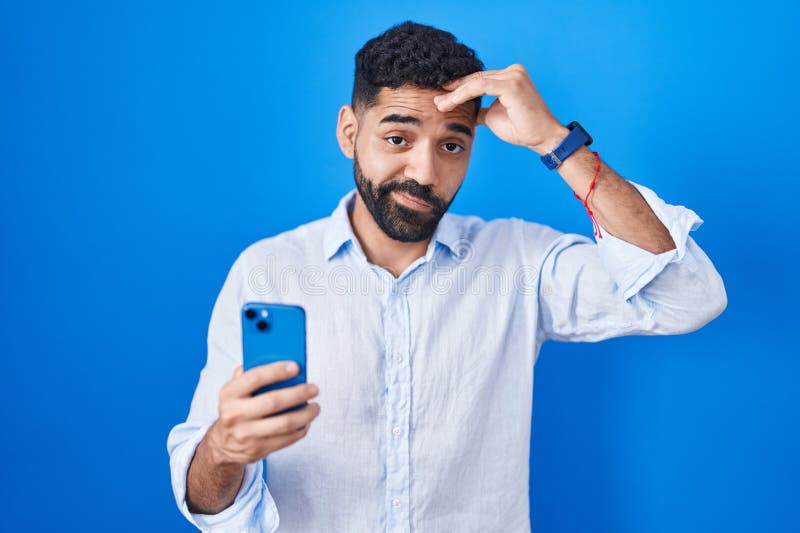Hispanic Man With Beard Using Smartphone Typing Message Worried And