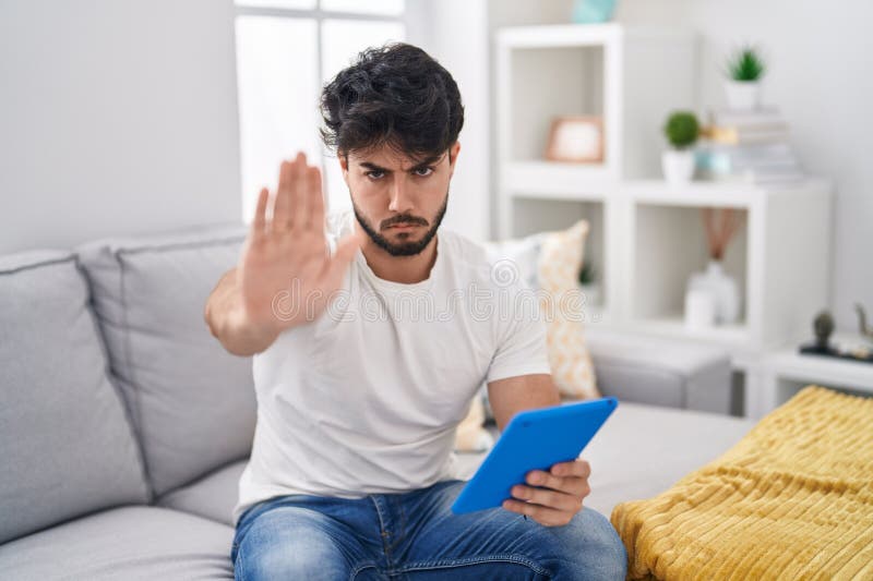 Hispanic Man with Beard Using Touchpad Sitting on the Sofa Doing Stop ...