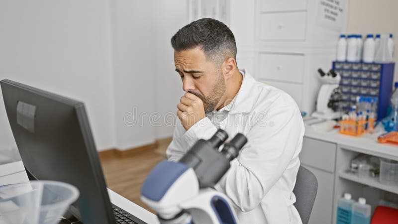 Hispanic Man in Lab Coat Deep in Thought at a Clinic Workstation with ...