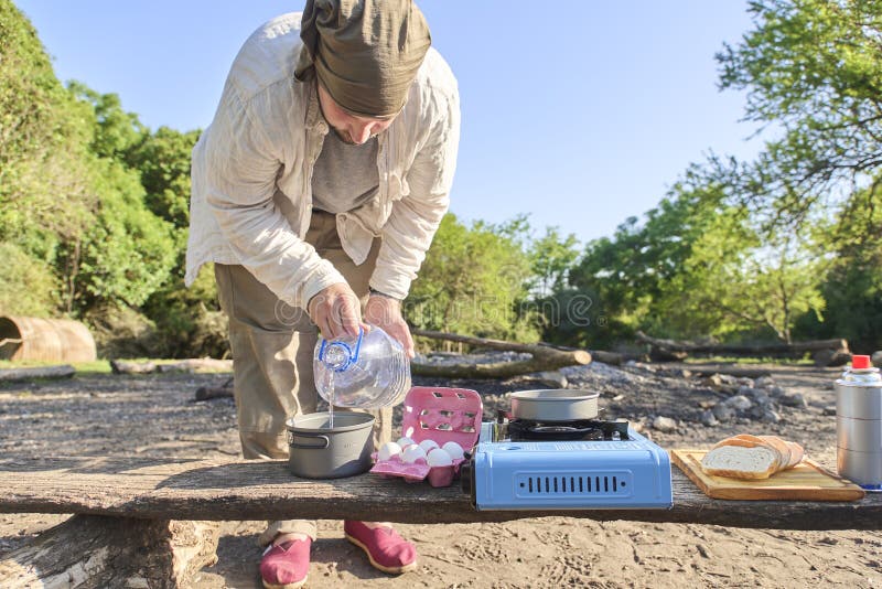 Hispanic Man Pouring Water into a Pot, Cooking Breakfast while Camping ...