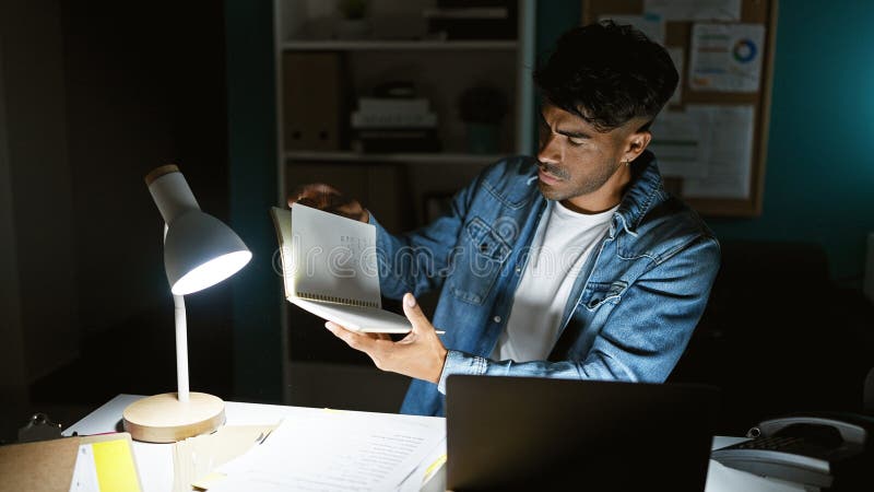 Hispanic Man Reading Notebook in a Dimly Lit Office at Night Stock ...