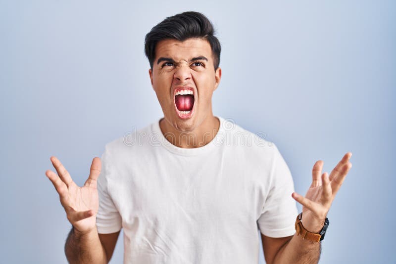 Hispanic Man Standing Over Blue Background Crazy and Mad Shouting and ...