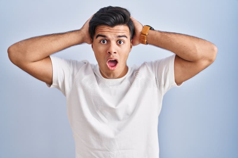 Hispanic Man Standing Over Blue Background Crazy and Scared with Hands ...