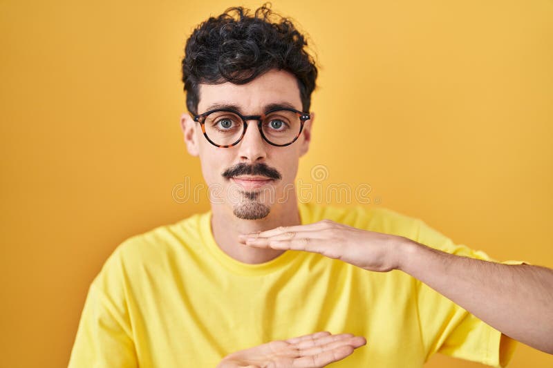 Hispanic Man Wearing Glasses Standing Over Yellow Background Gesturing