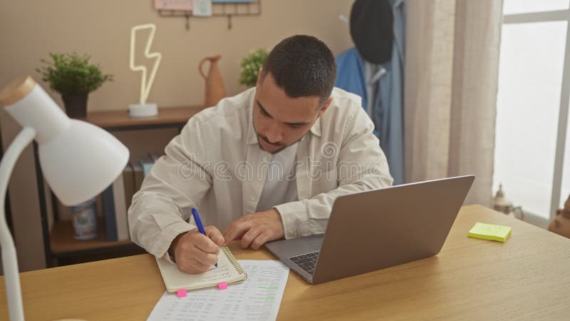 Hispanic Man Working on Laptop and Writing Notes, Portraying Modern ...