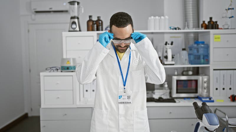 Hispanic Scientist in Lab Coat Adjusting Safety Goggles in a Modern ...