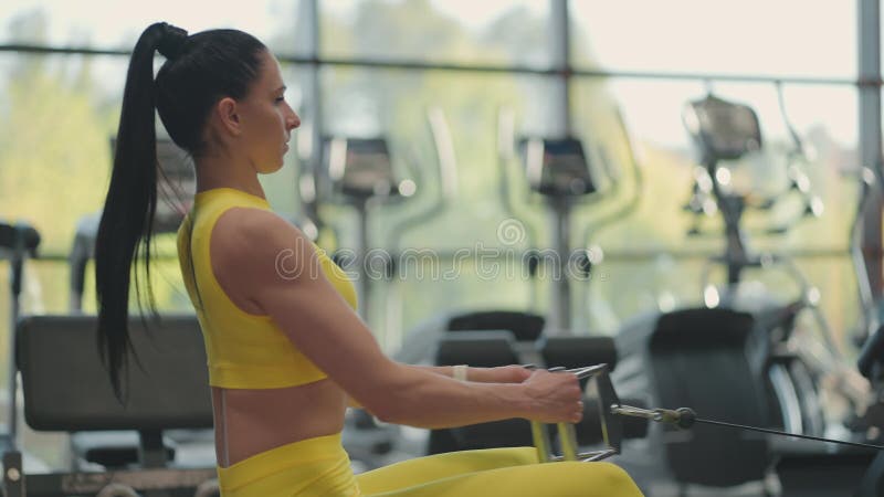 Hispanic Woman Does Exercises On The Rowing Machine A Girl Sits Behind