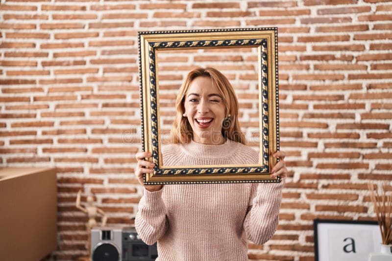 Hispanic Woman Holding Empty Frame Winking Looking at the Camera with ...