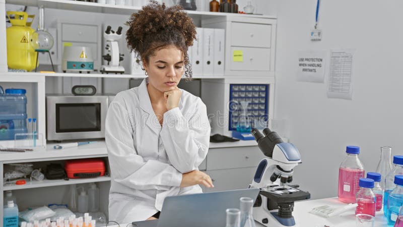 Hispanic Woman Working Thoughtfully in a Laboratory with Microscope and ...