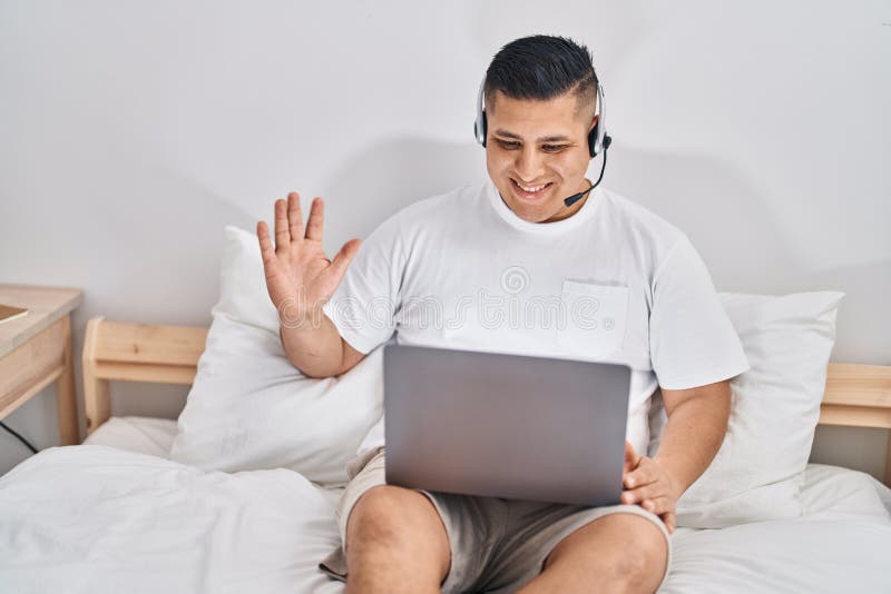 Hispanic Young Man Using Computer Laptop on the Bed Looking Positive ...