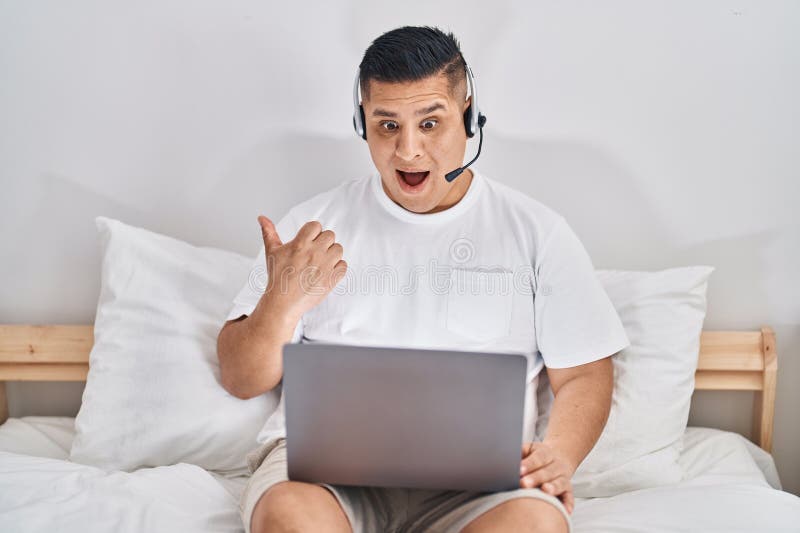 Hispanic Young Man Using Computer Laptop on the Bed Pointing Thumb Up ...