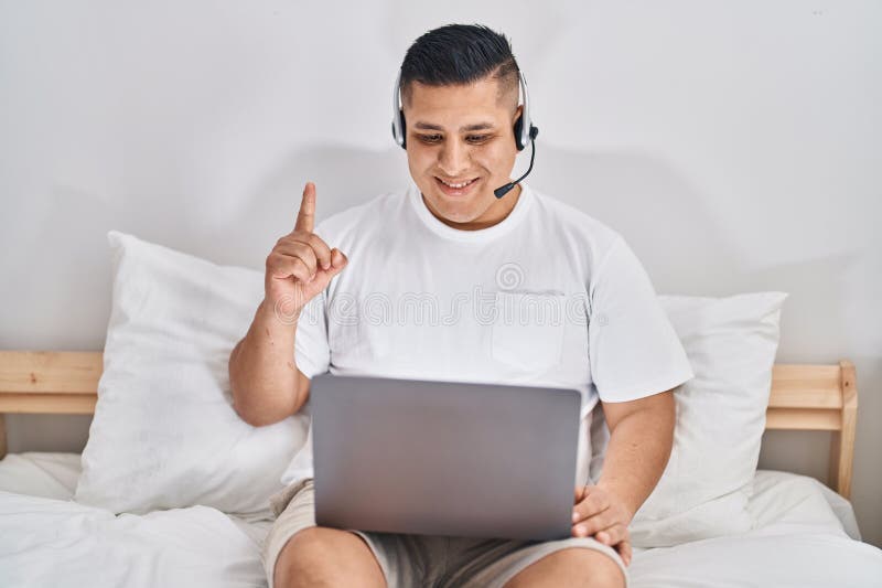 Hispanic Young Man Using Computer Laptop on the Bed Smiling with an ...