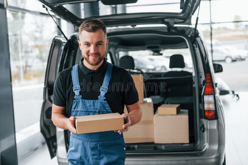 Holding Box. Delivery Man in Uniform is Indoors with Car and with Order ...