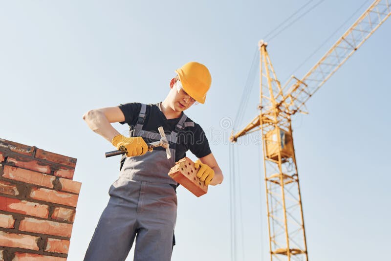 Holding Brick and Using Hammer. Construction Worker in Uniform and ...
