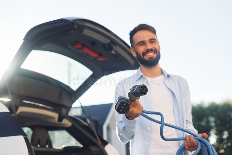 Holding Charging Cable. Young Stylish Man is with Electric Car at ...