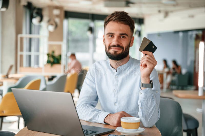 Holding Credit Cards. Young Man is Sitting in the Cafe and Working by ...