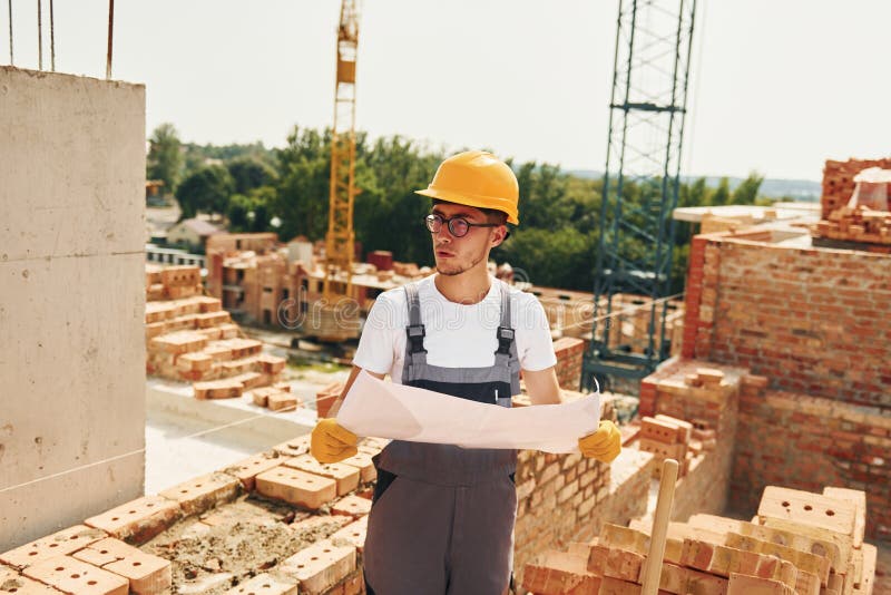 Holding Document. Young Construction Worker in Uniform is Busy at the Unfinished Building Stock ...