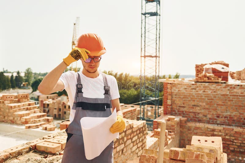 Holding Document. Young Construction Worker in Uniform is Busy at the Unfinished Building Stock ...