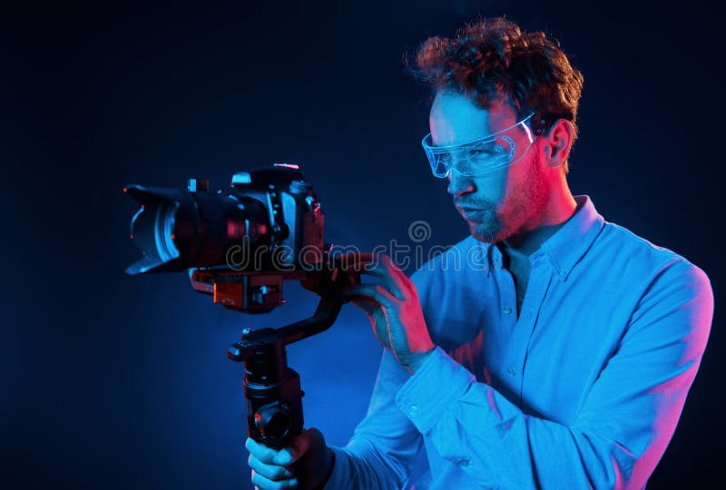 Holds Camera. Neon Lighting. Young European Man is in the Dark Studio ...