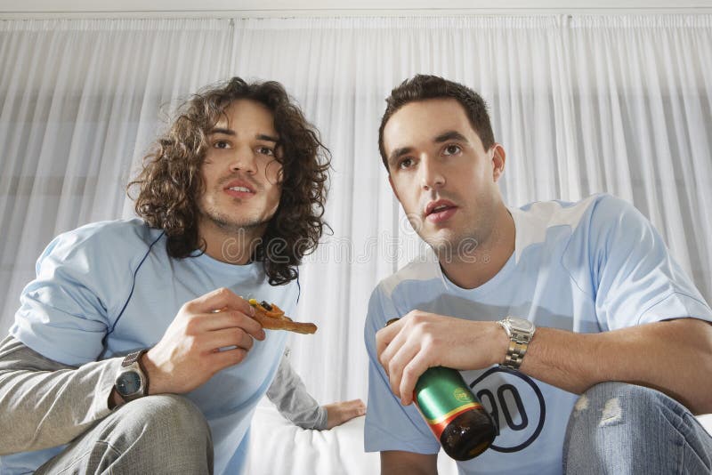 Hombres Serios Que Ven La TV Y Que Comen Pizza Con La Cerveza Foto de ... Hombres Serios Que Ven La TV Y Que Comen Pizza Con La Cerveza Foto de ...