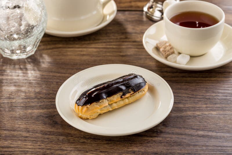 Homemade Eclair Dessert with Chocolate Sauce and Cup of Tea on Wooden ...
