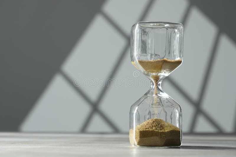 Hourglass with Flowing Gold Sand on Table Against White Wall, Space for ...