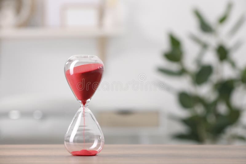 Hourglass with Red Flowing Sand on Table Against Blurred Background ...
