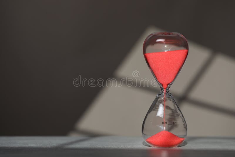 Hourglass with Red Flowing Sand on Table Against Light Grey Background ...