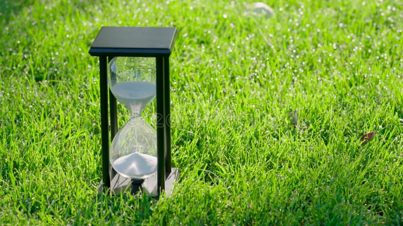 An Hourglass with Spilling Sand Standing on Green Grass with Glittering ...