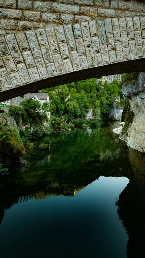 House and Trees Reflected on a River with Clear Water Under a Bridge ...