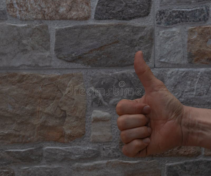 Human Hand Displays a Thumbs Up Sign Against a Textured Stone Wall ...