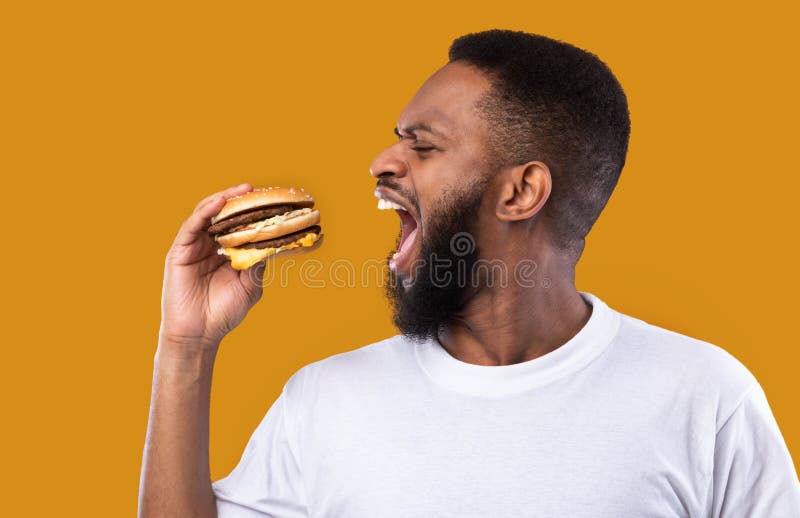Hungry African Guy Biting Burger Posing on Yellow Background, Side-View ...