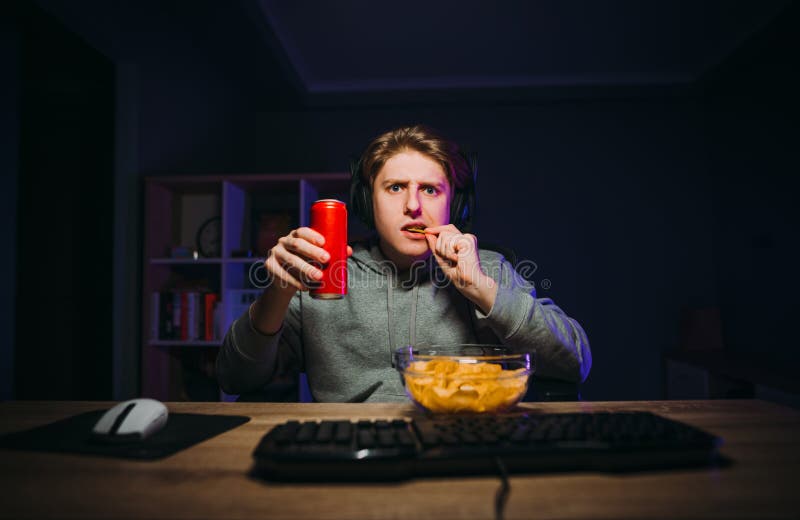 A Hungry Gamer in a Headset Eats Chips and Drinks Sweet Water with a ...